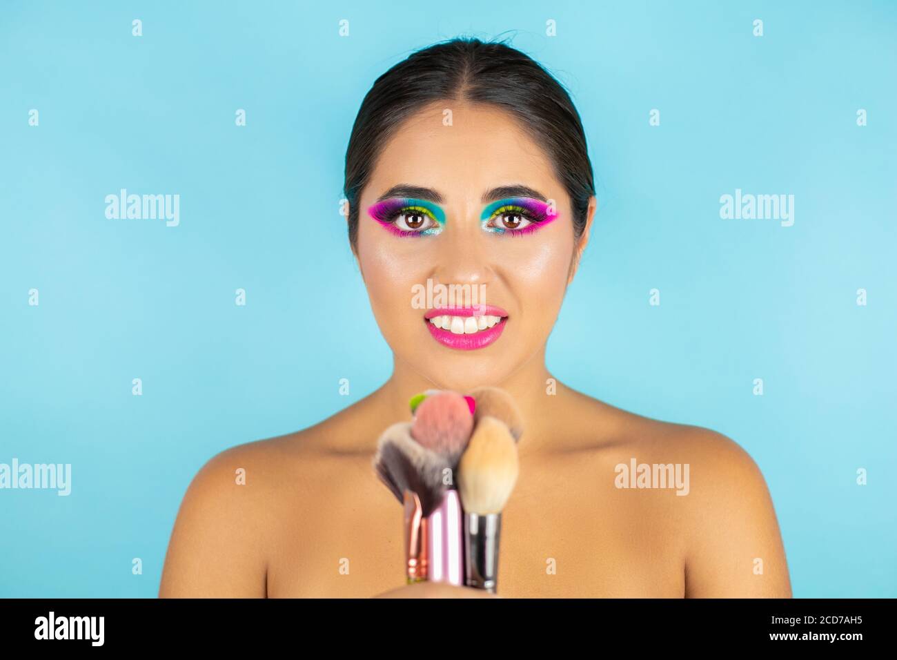 Beauty portrait of female model with vivid makeup and brushes on blue ...
