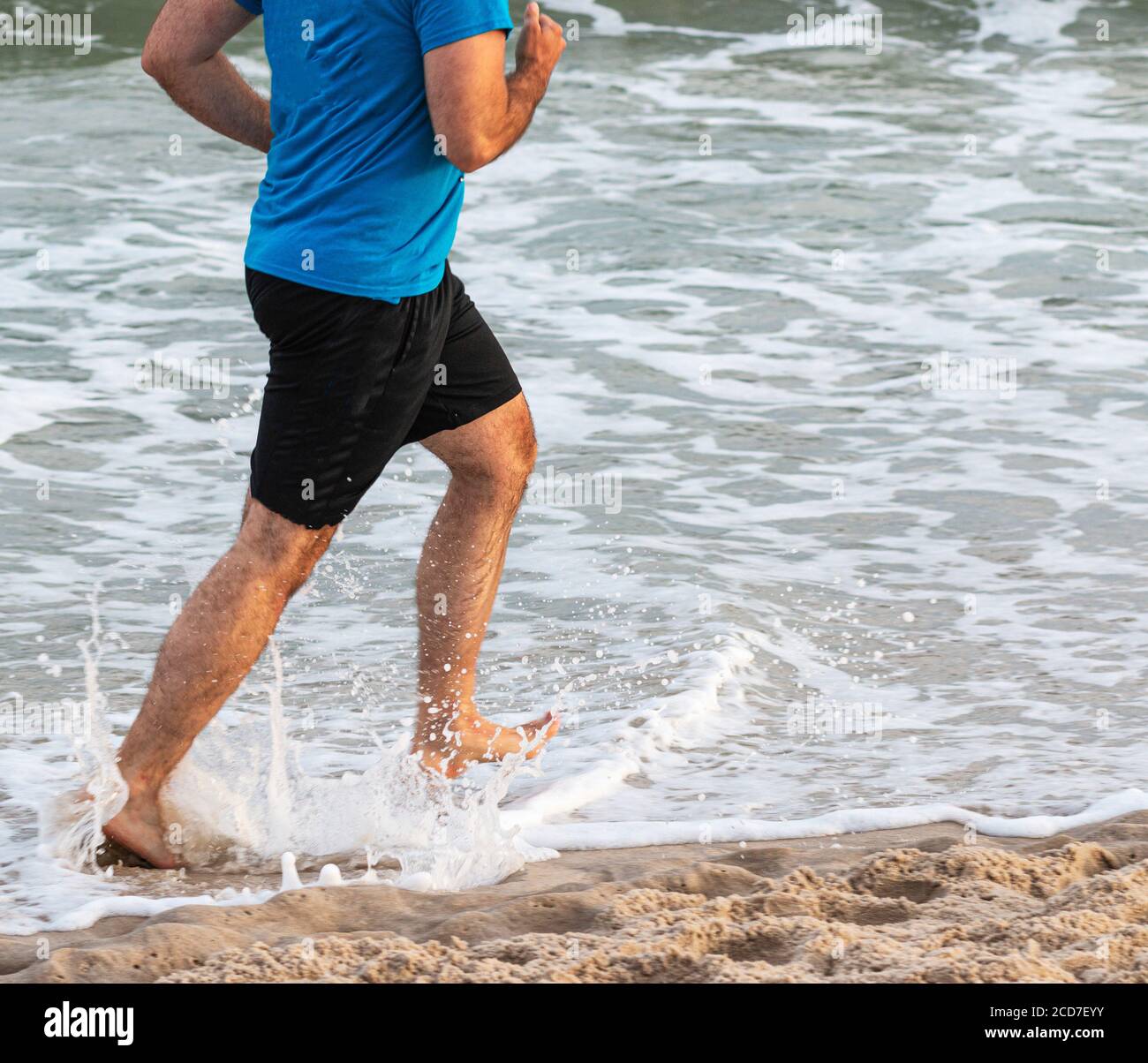 Side view of a man is running in the ocean on the waters edge barefoot ...