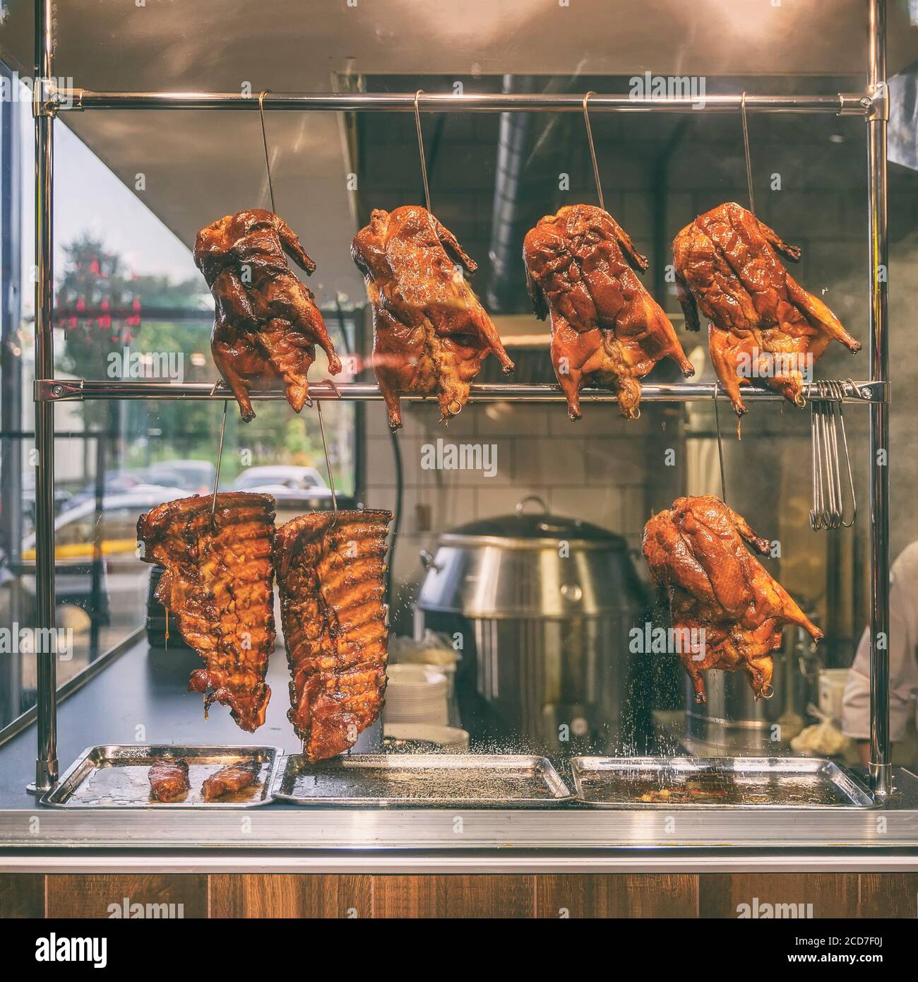 Roasted ducks and ribs hanging on rack showcase in restaurant's kitchen ...