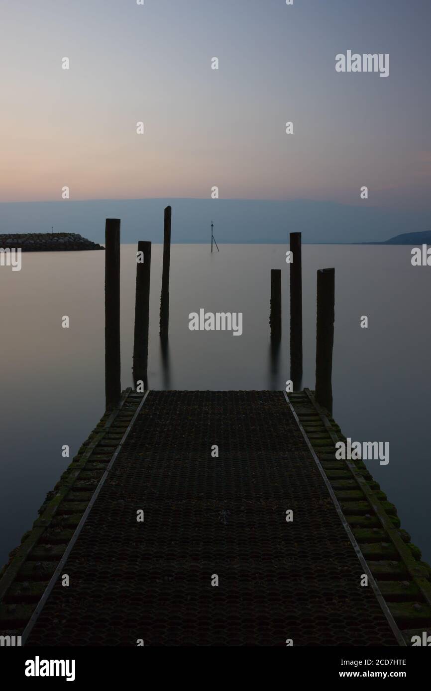 Small jetty in a North Wales harbour. Flat summer sea at dawn in Rhos ...