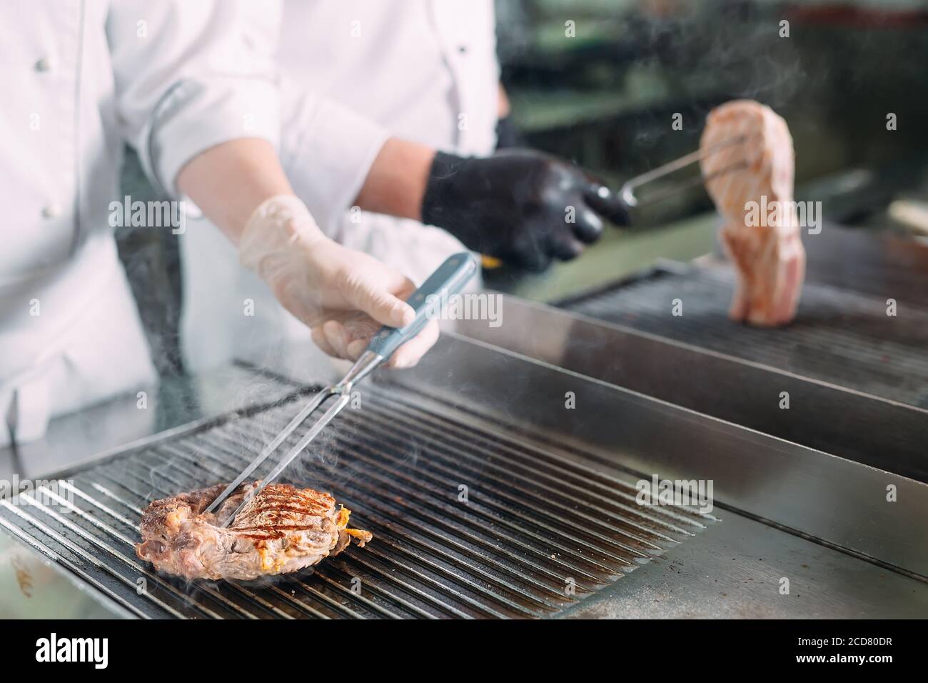 Cooks roast meat on the stove in the kitchen of a restaurant or hotel ...