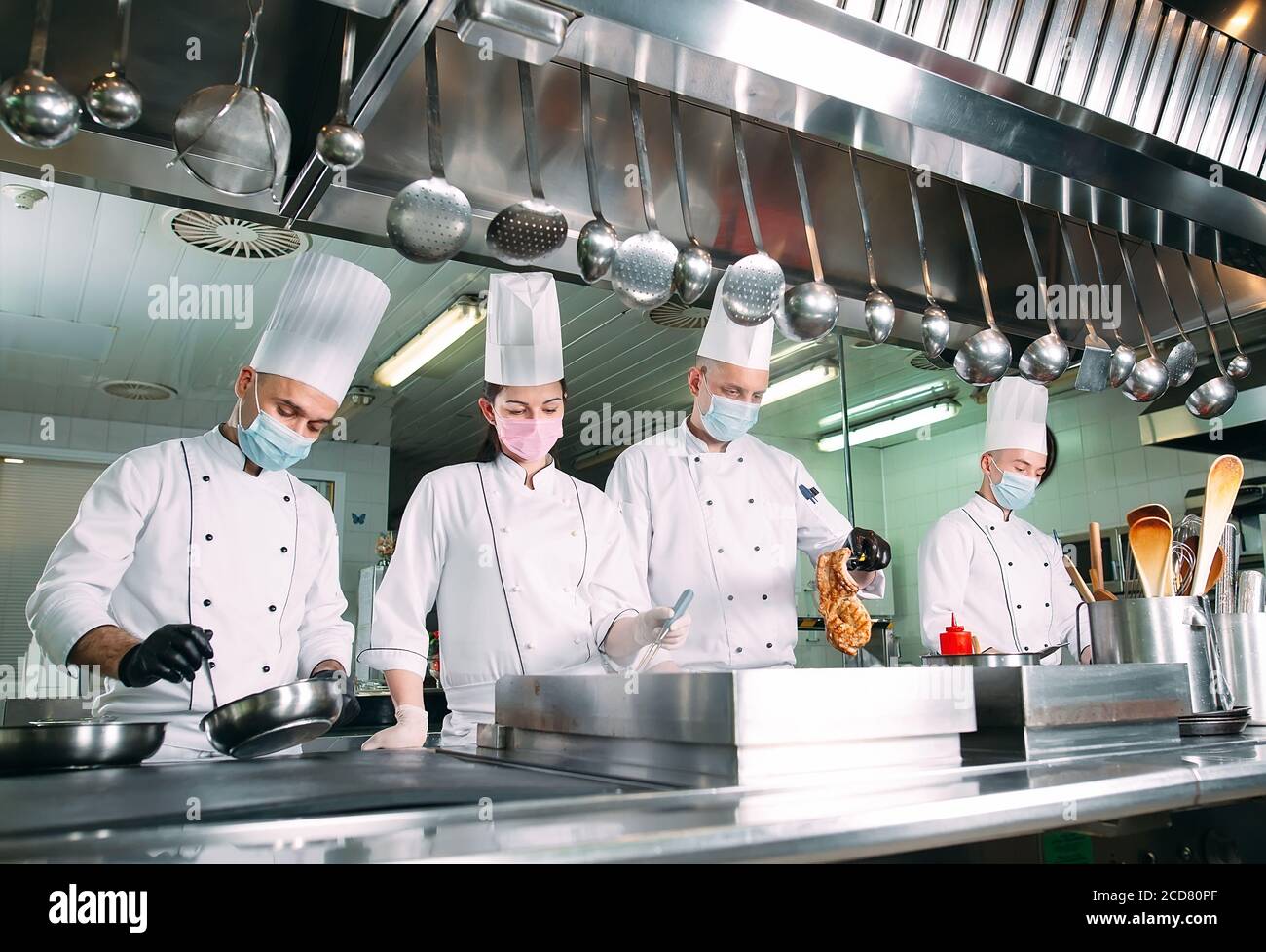 Chefs in protective masks and gloves prepare food in the kitchen of a ...