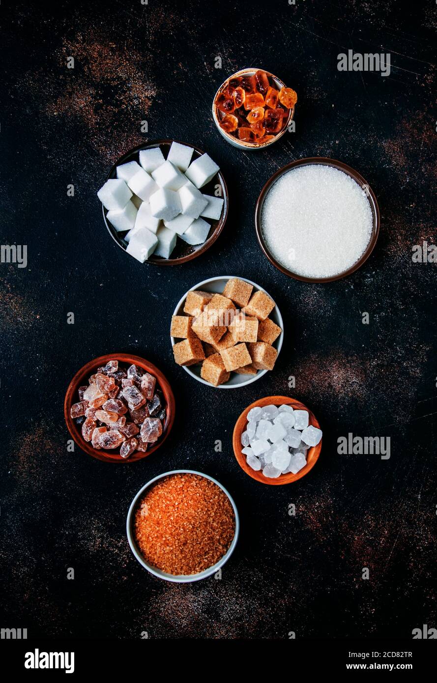Assorted different types of sugar in bowls on a table on a dark ...