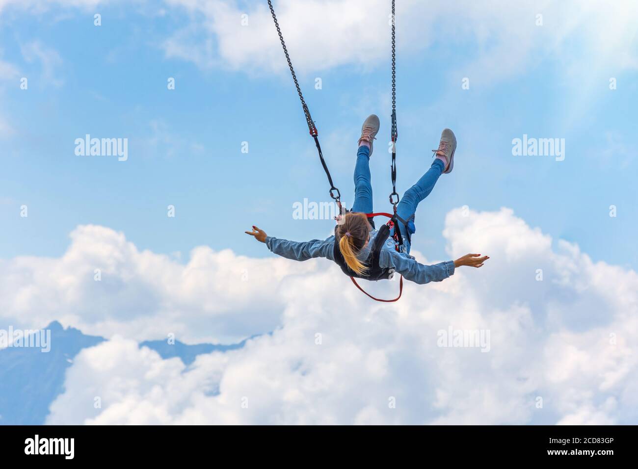 Girl swinging on a hanging swing over an abyss against the backdrop of ...