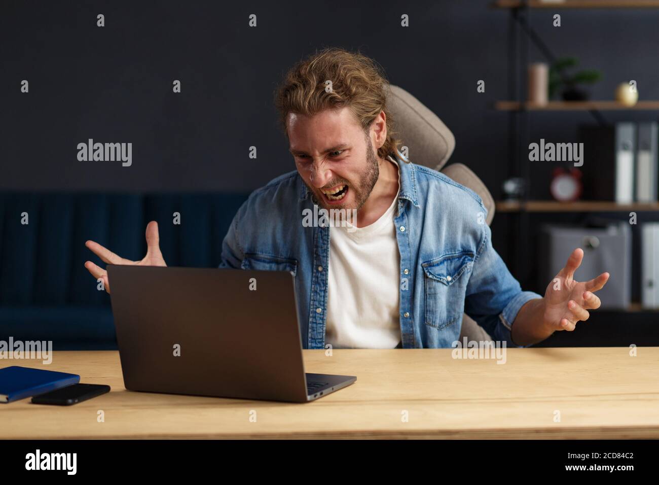 Angry young handsome curly man using laptop. Stressed freelancer lost ...