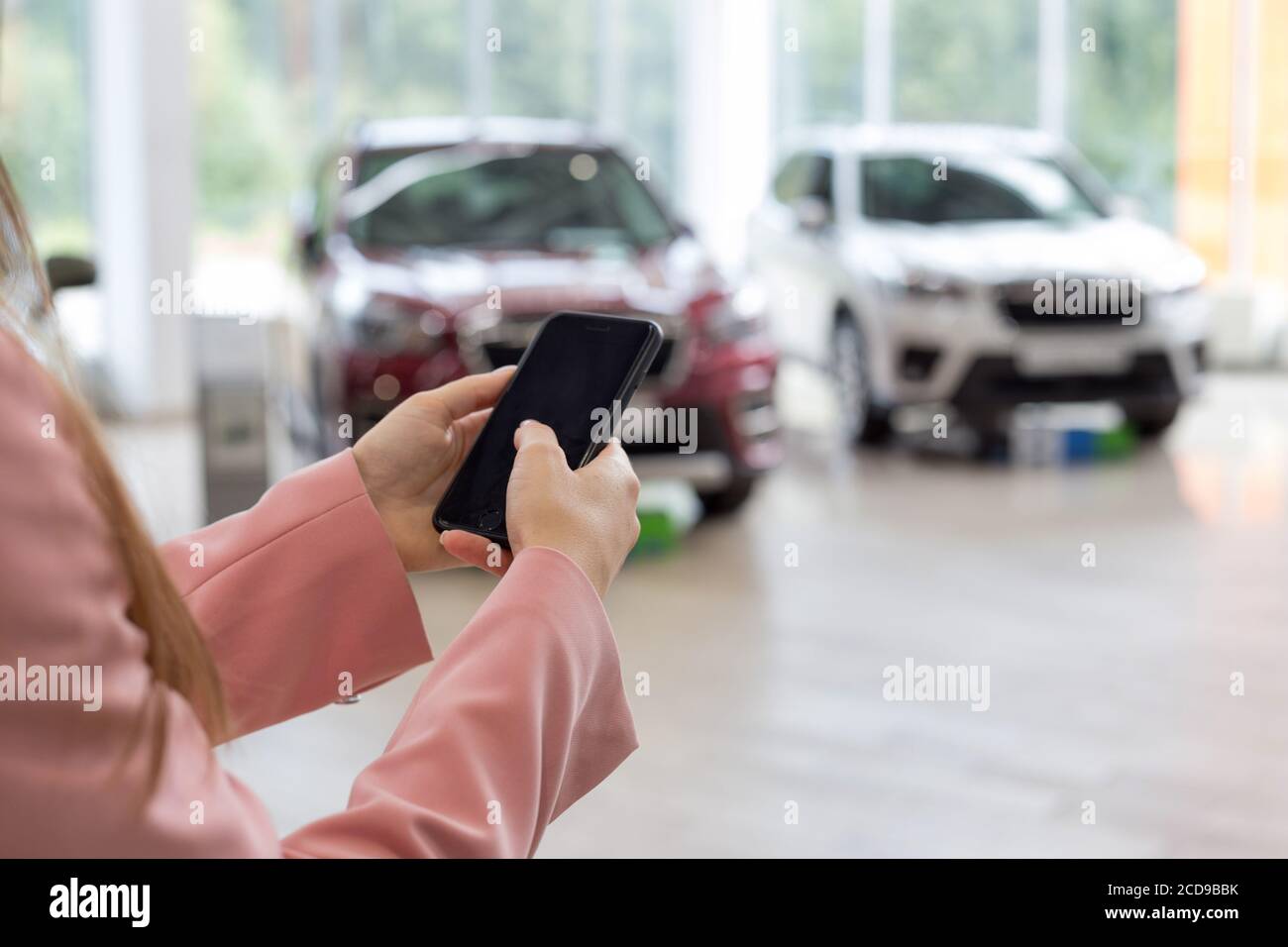Saleswoman using mobile smart phone at dealer showroom. Modern working ...