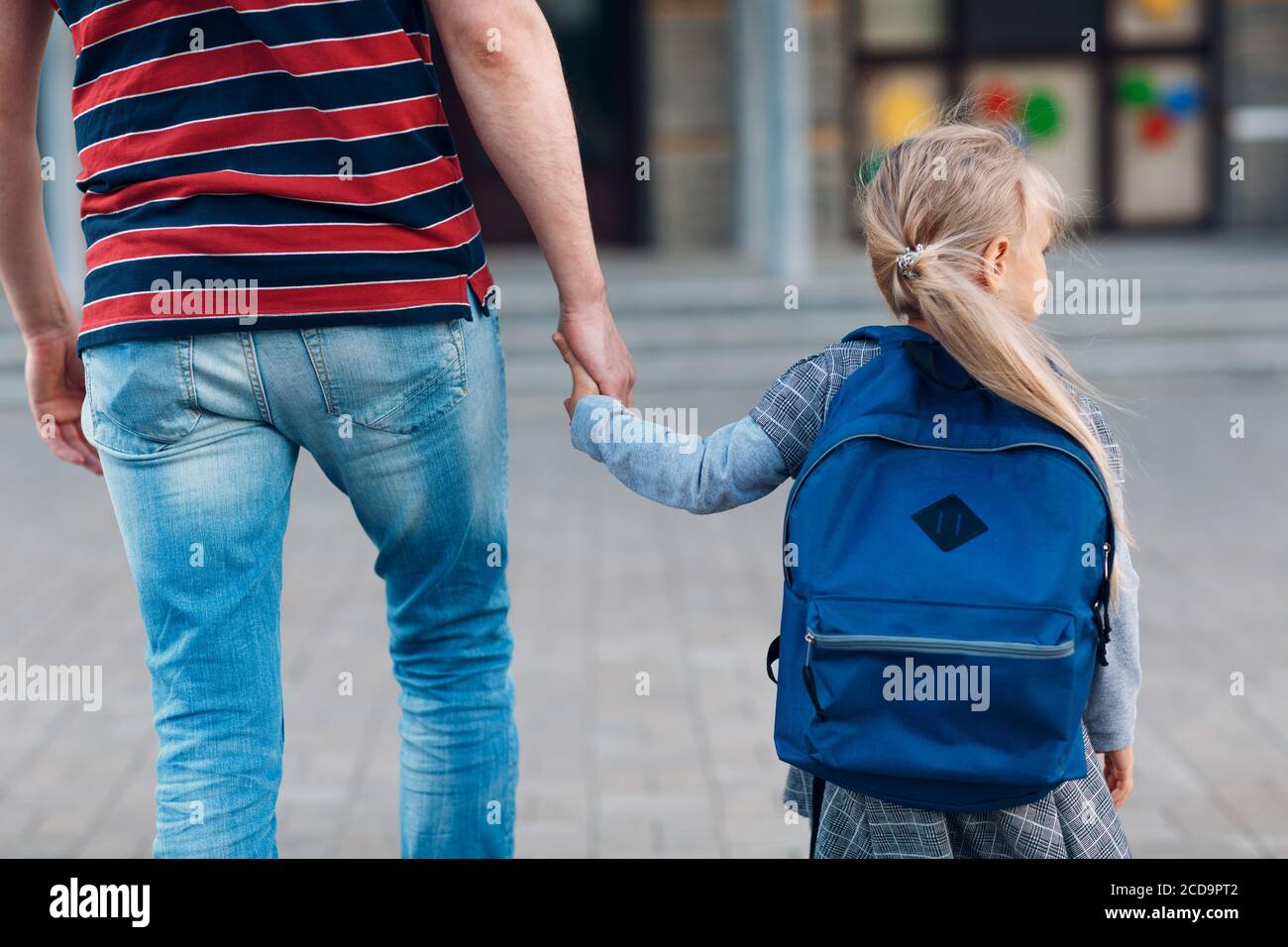 Rear view of father walking back to school with his daughter carrying ...