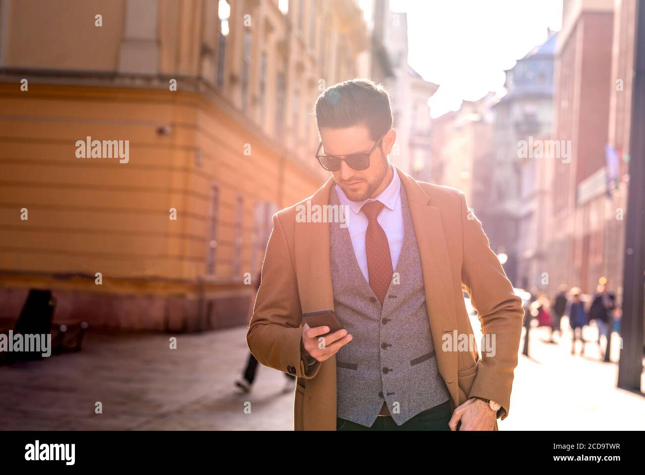 A handsome elegant man walking on the streets and using his smartphone ...