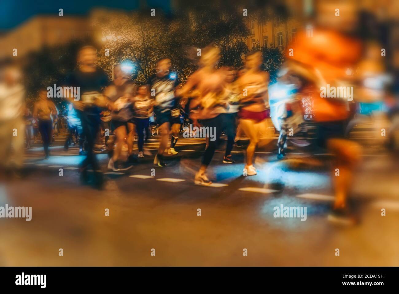 Large group of running athletes on street, night city marathon, blur ...