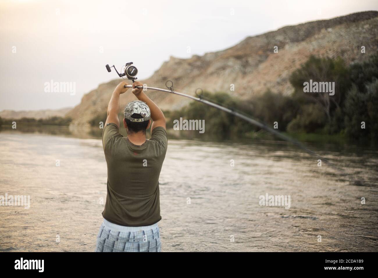 Back view of a person fishing in a lake with a rod Stock Photo - Alamy