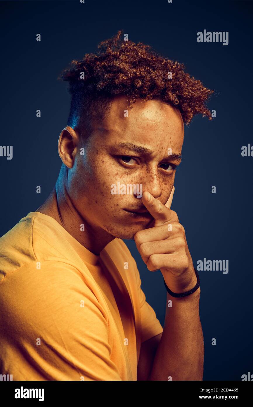 Freestyle. Mulatto guy standing isolated on dark red in yellow light ...