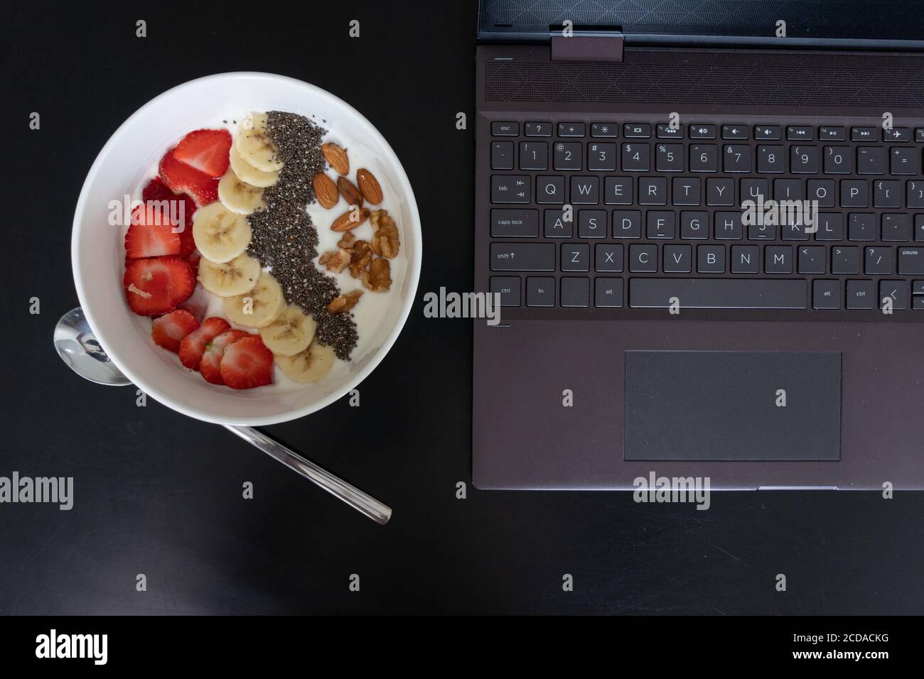 Top view of a bowl of yogurt with fruits on the table with a laptop on ...