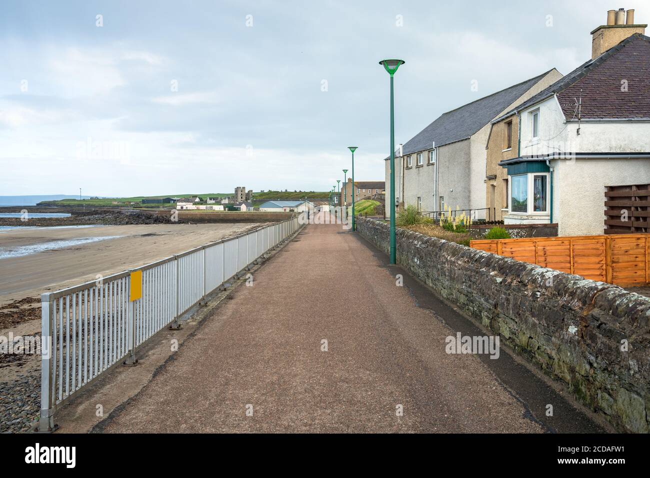 Deserted paved path along a beach with houses on the right side on a ...