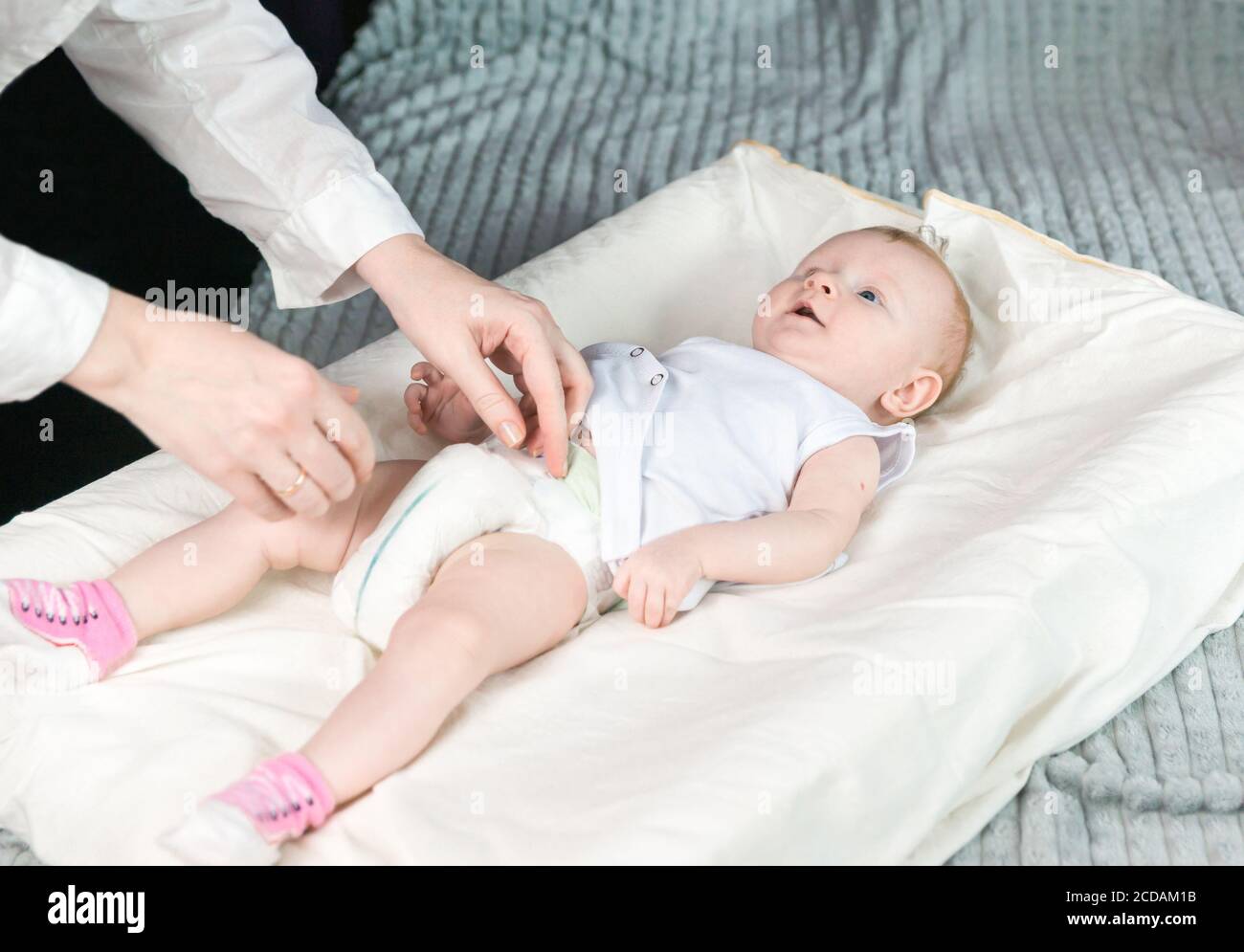 Mom changes the babys diaper. The baby is lying on the changing table ...