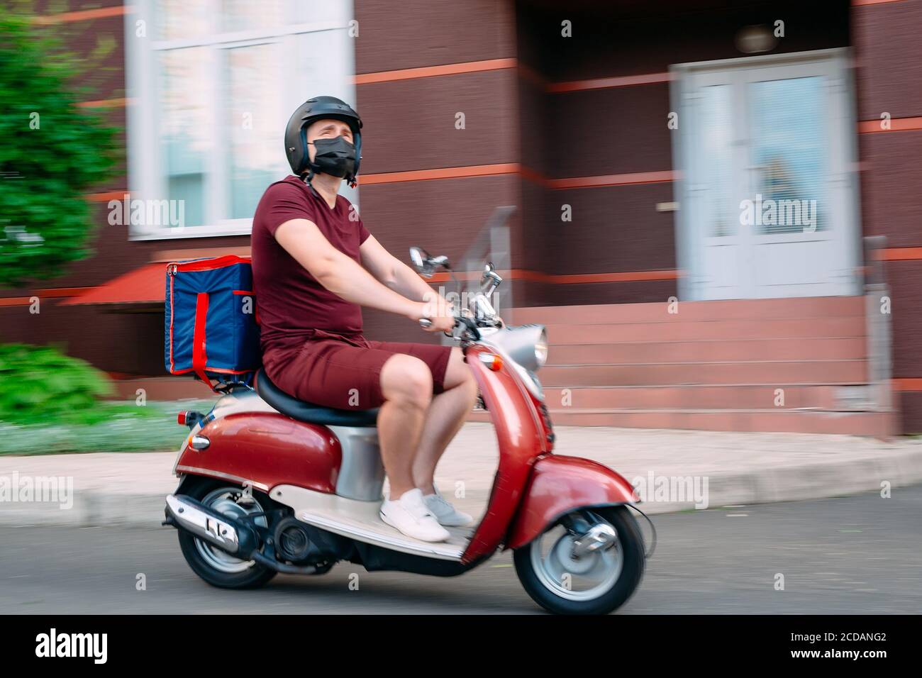 Delivery boy wearing red uniform on scooter with isothermal food case ...