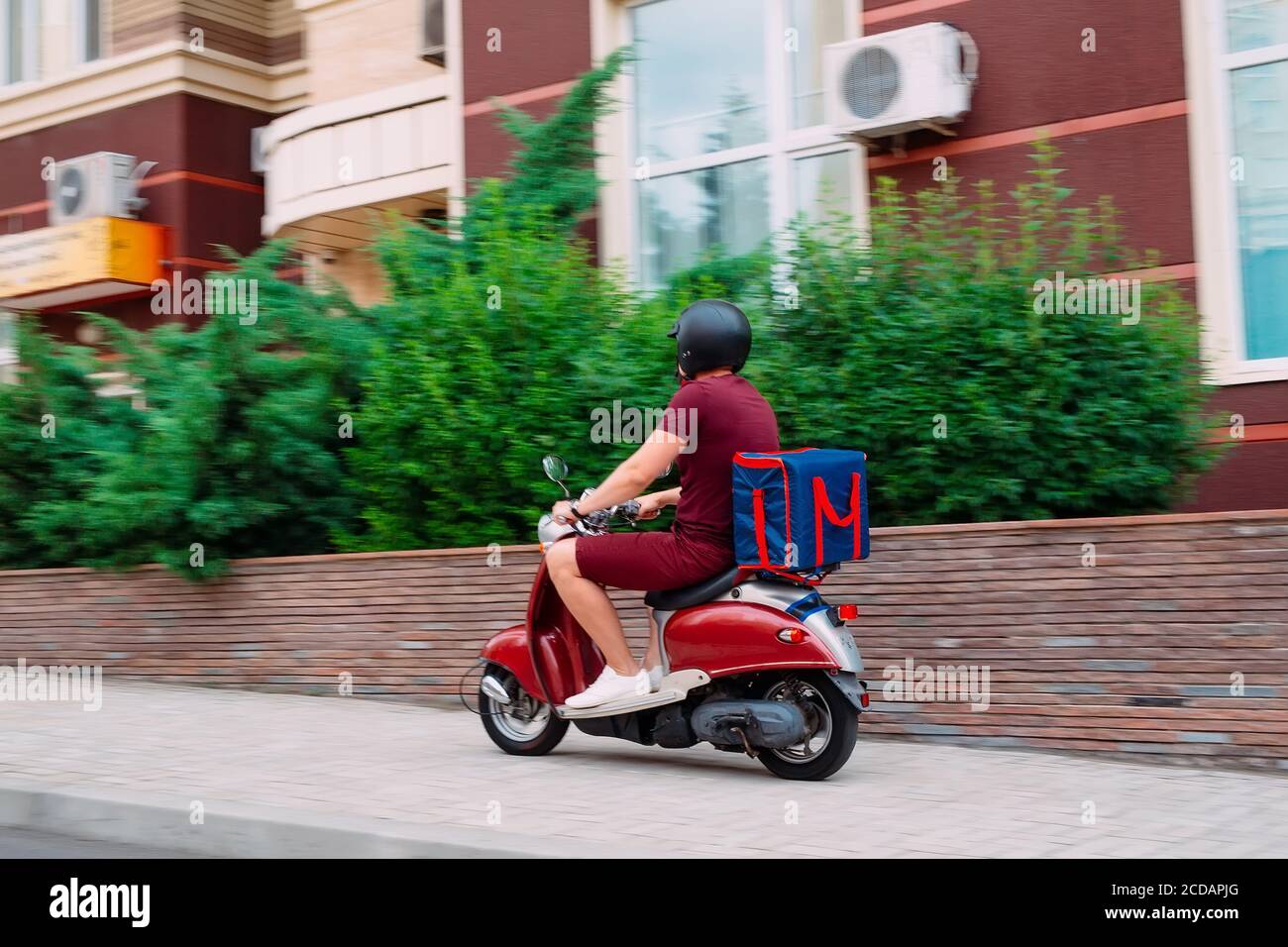 Delivery boy wearing red uniform on scooter with isothermal food case ...