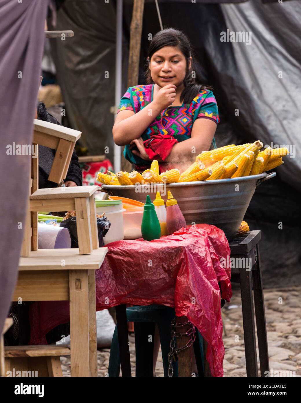 A young Quiche Mayan woman in traditional dress sells elote or steamed ...