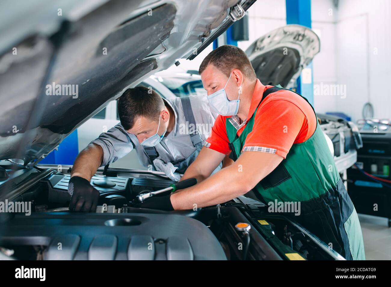 Mechanics in uniform and protective masks work in a car workshop Stock ...