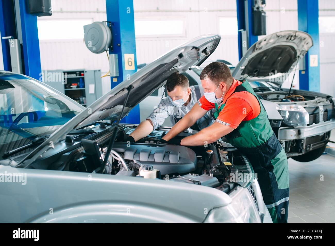 Mechanics in uniform and protective masks work in a car workshop Stock ...