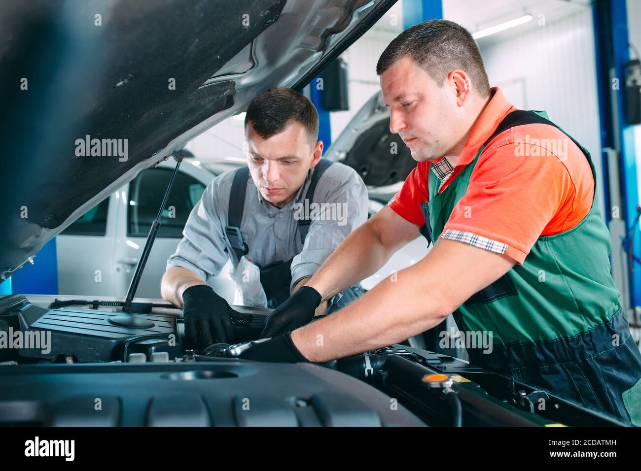 Two handsome mechanics in uniform are working in auto service. Car ...