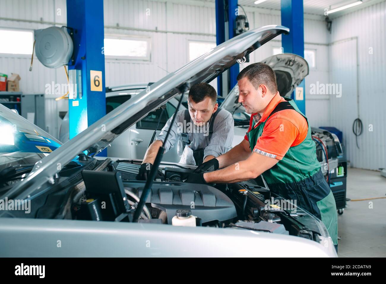 Two handsome mechanics in uniform are working in auto service. Car ...