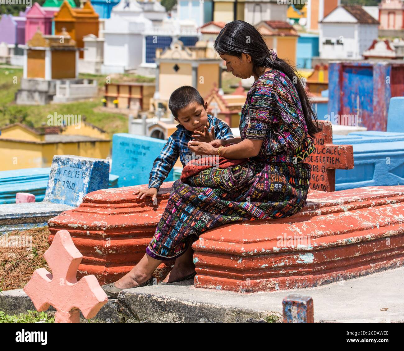 A Mayan mother and son sit on a gravestone in the colorful cemetery in ...