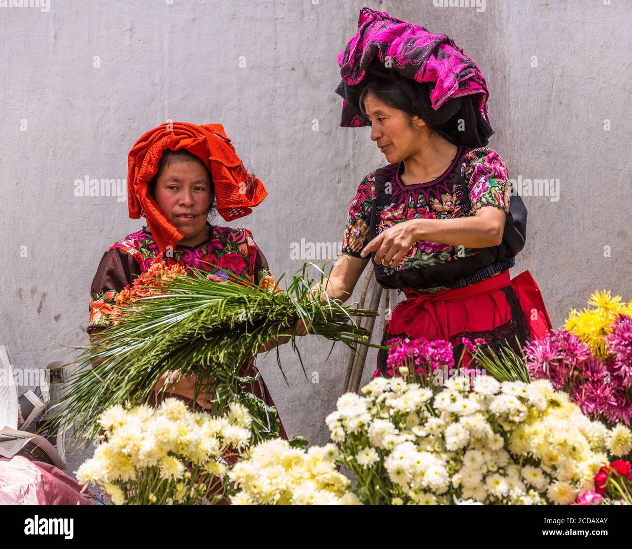 Two Quiche Mayan woman in traditional dress sell flowers in the market ...