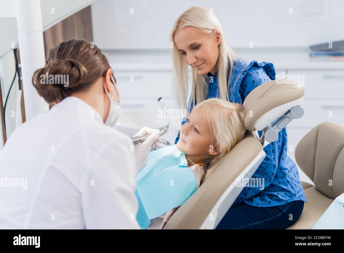 A mother watching a dentist taking care of her little daughter's teeth ...
