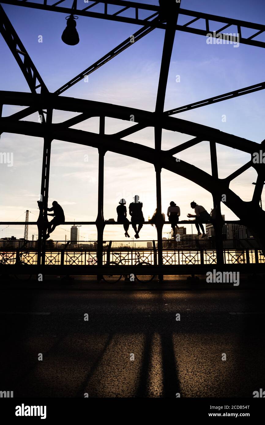 Unidentifiable backlit people enjoying the sunset sitting on a steel ...