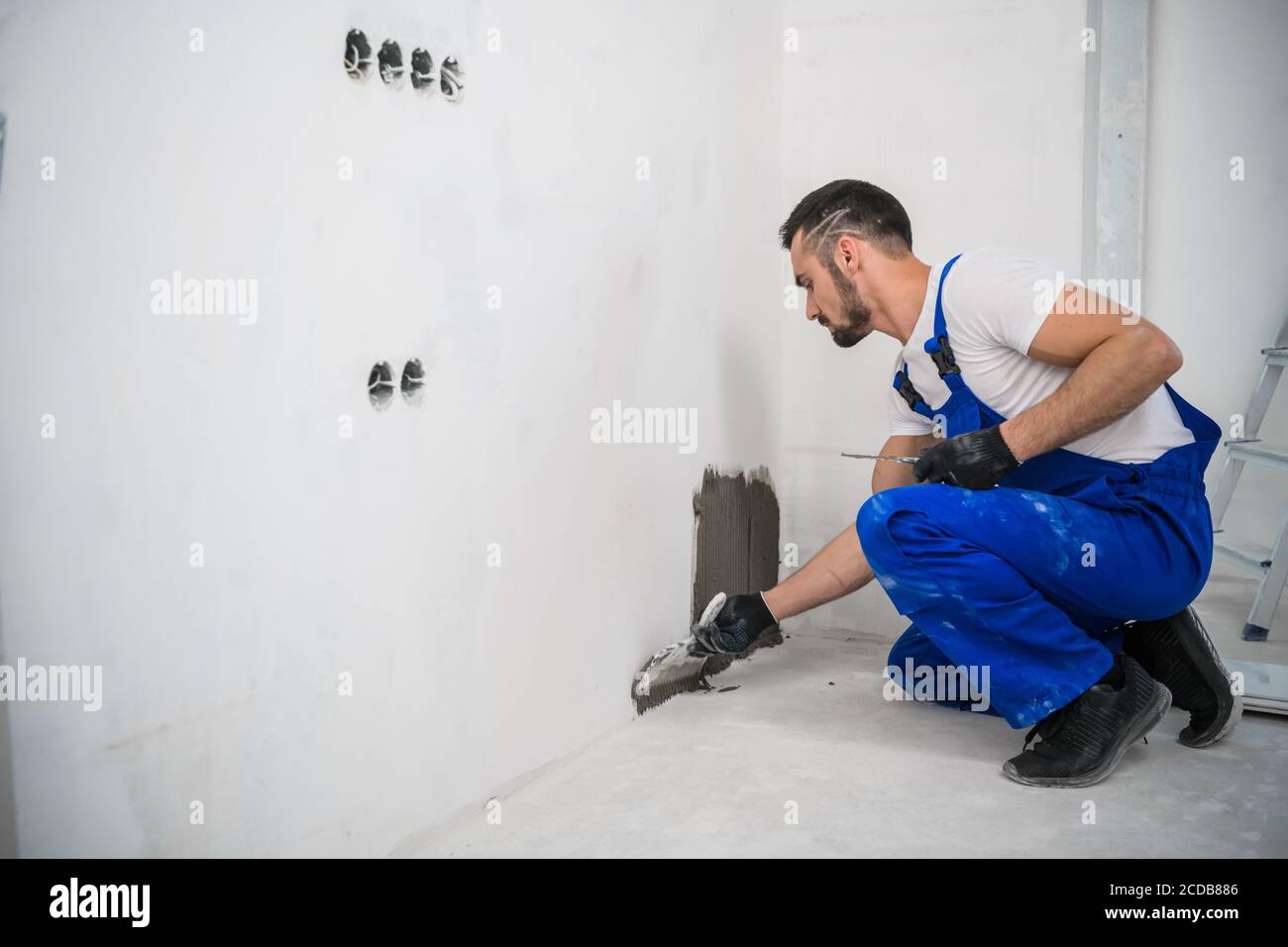 A man in overalls uses a trowel to cover the wall with cement Stock ...