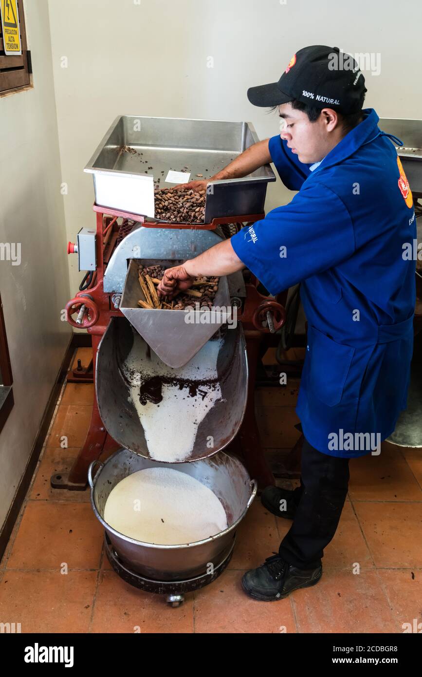 A worker puts roasted cacao beans and cinnamon sticks in a machine for ...