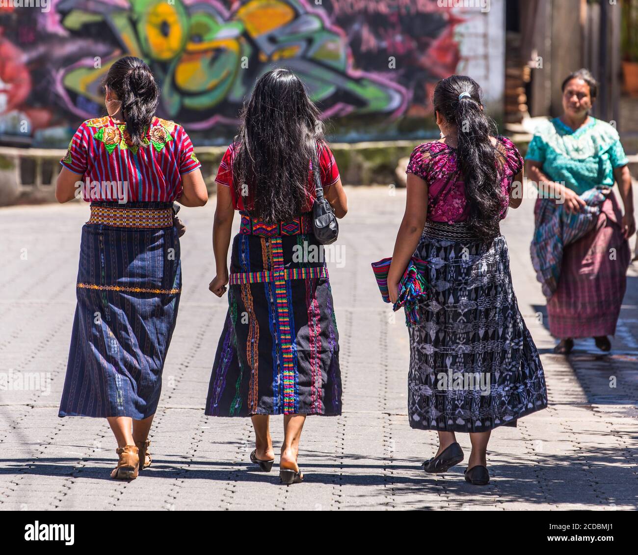 Three young Tzutujil Mayan women in traditional dress walk along a ...