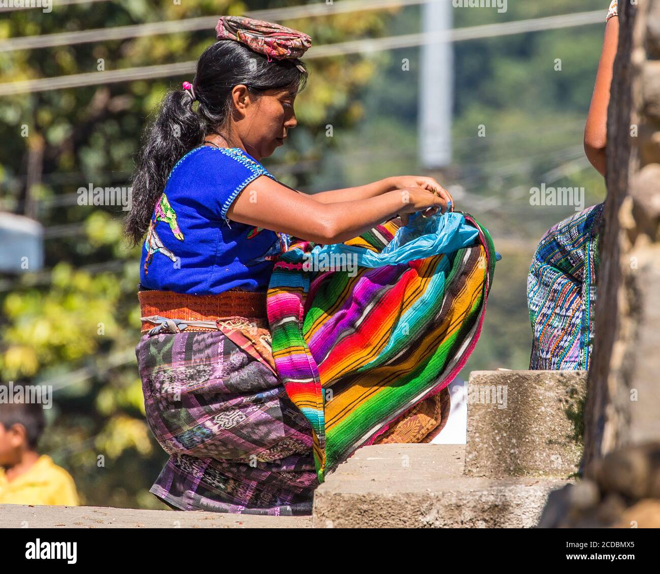 A young Tzutujil Mayan woman in traditional dress kneels on a street in ...