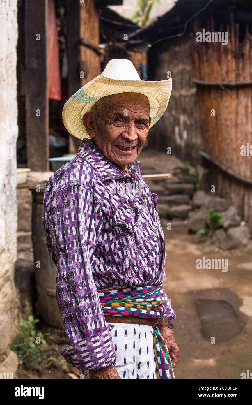 90 year old Mayan man in traditional dress stands in front of his home ...