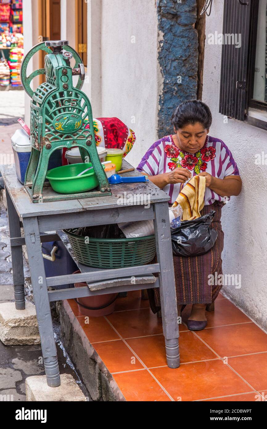 A Mayan woman wearing traditional dress sews as she waits for customers ...