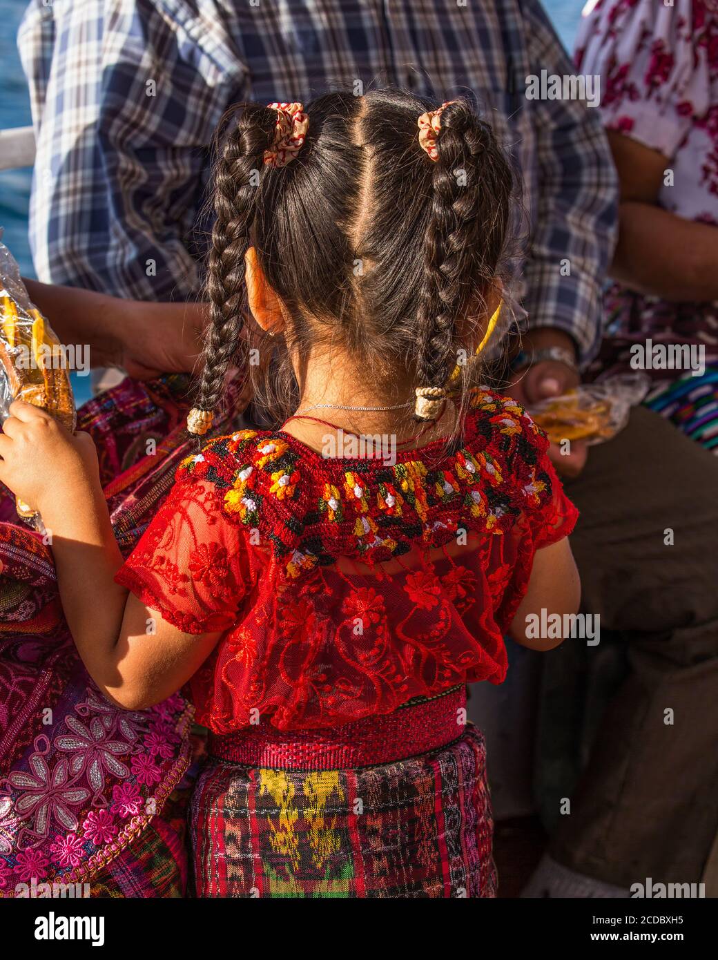 A young Tzutujil Mayan girl in traditional dress holds a bag of dried ...