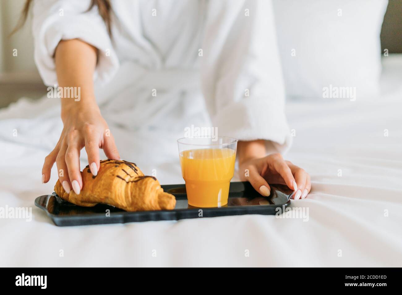 Young woman in white robe having breakfast orange juice and croissant ...
