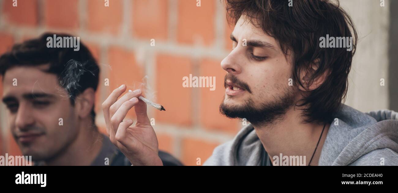 Closeup of young friends smoke pot or hashish joint in abandoned ghetto ...