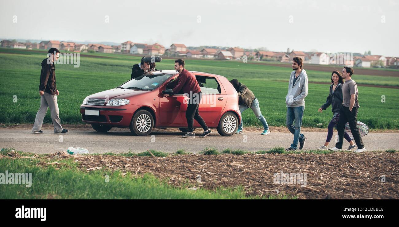 Behind scene improvisation. Film crew team pushing car while cameraman ...
