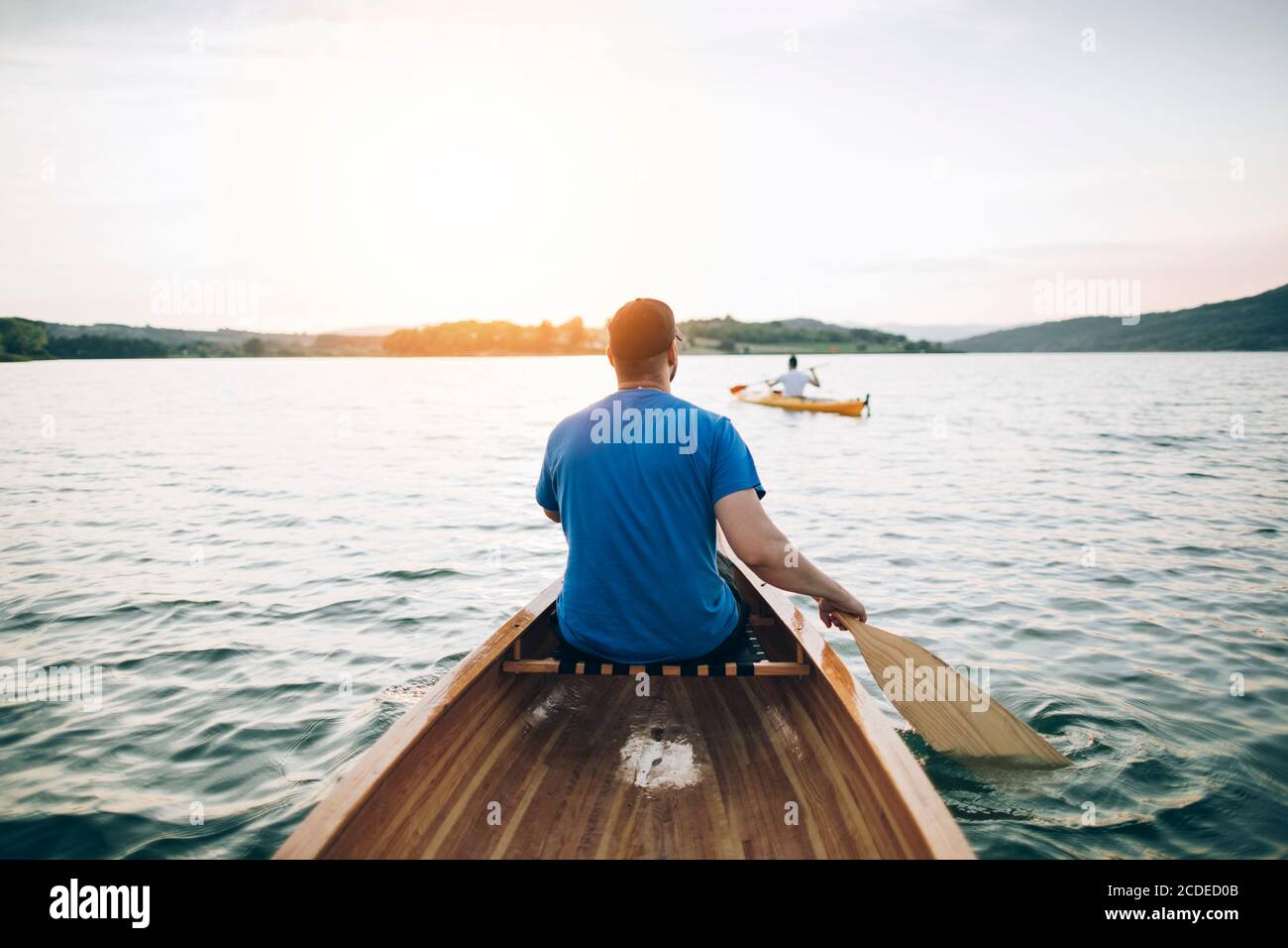 Rear view of men paddling canoe and kayak at sunset lake Stock Photo ...