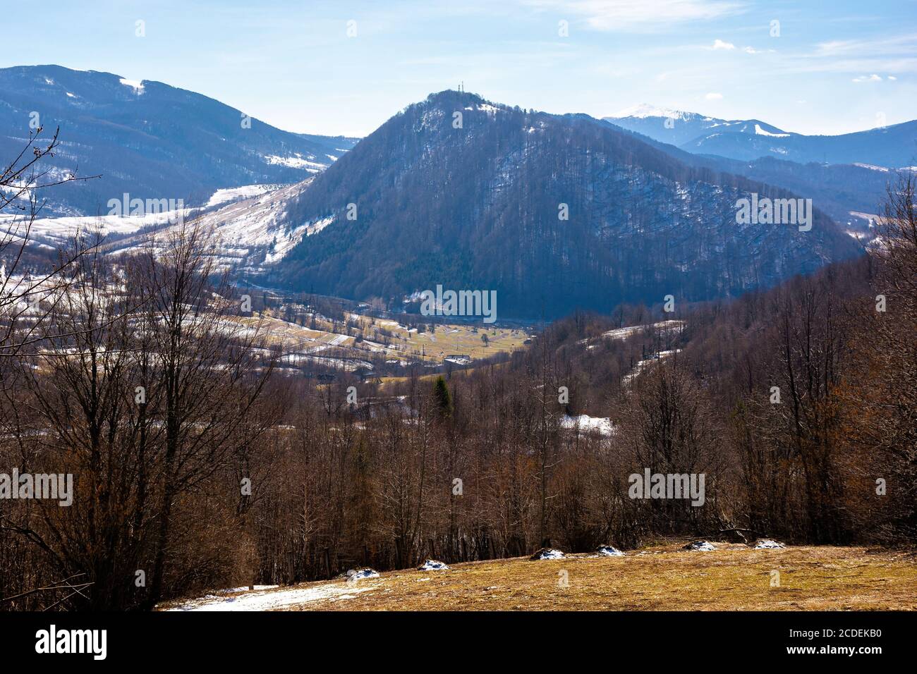 mountainous countryside in early spring. dry grass and leafless trees on the hillside. snow in ...