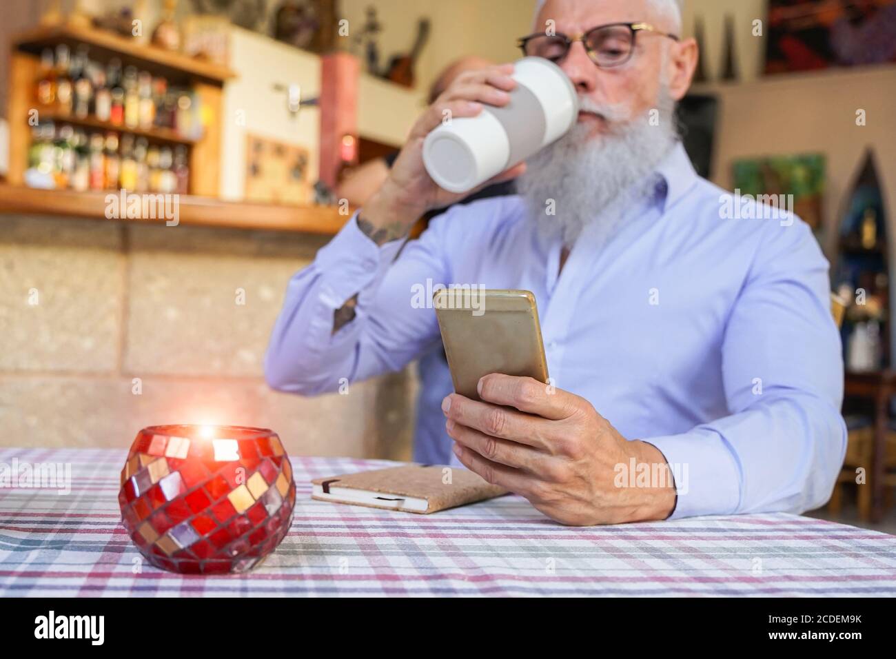 Senior man using smartphone app while drinking coffee. Old man using ...