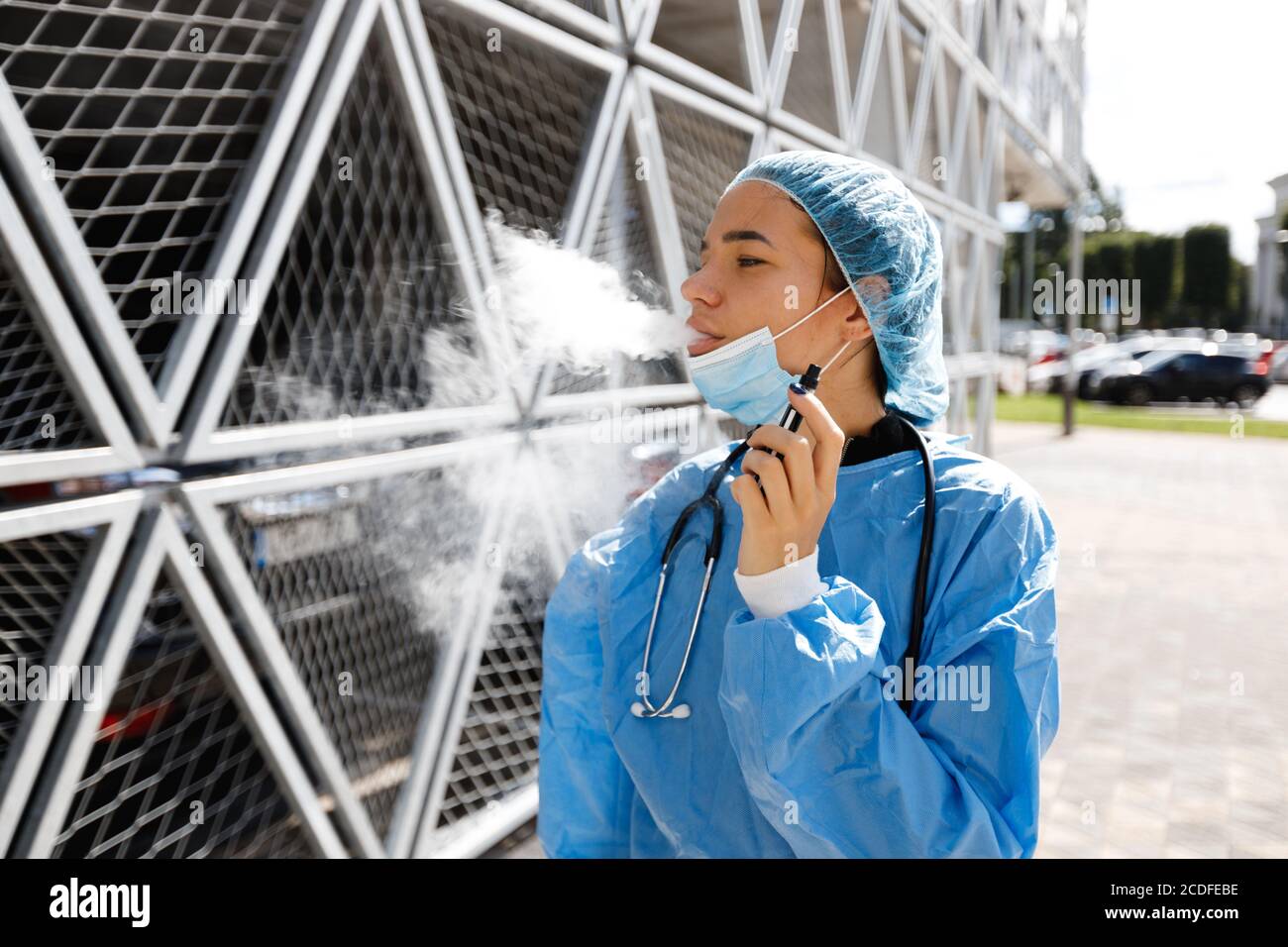 Tired young doctor or nurse on break after surgery smoking electronic ...