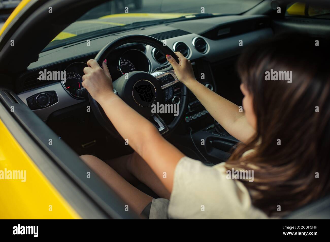 Girl sits behind the wheel of yellow car with the autobot logo on the ...