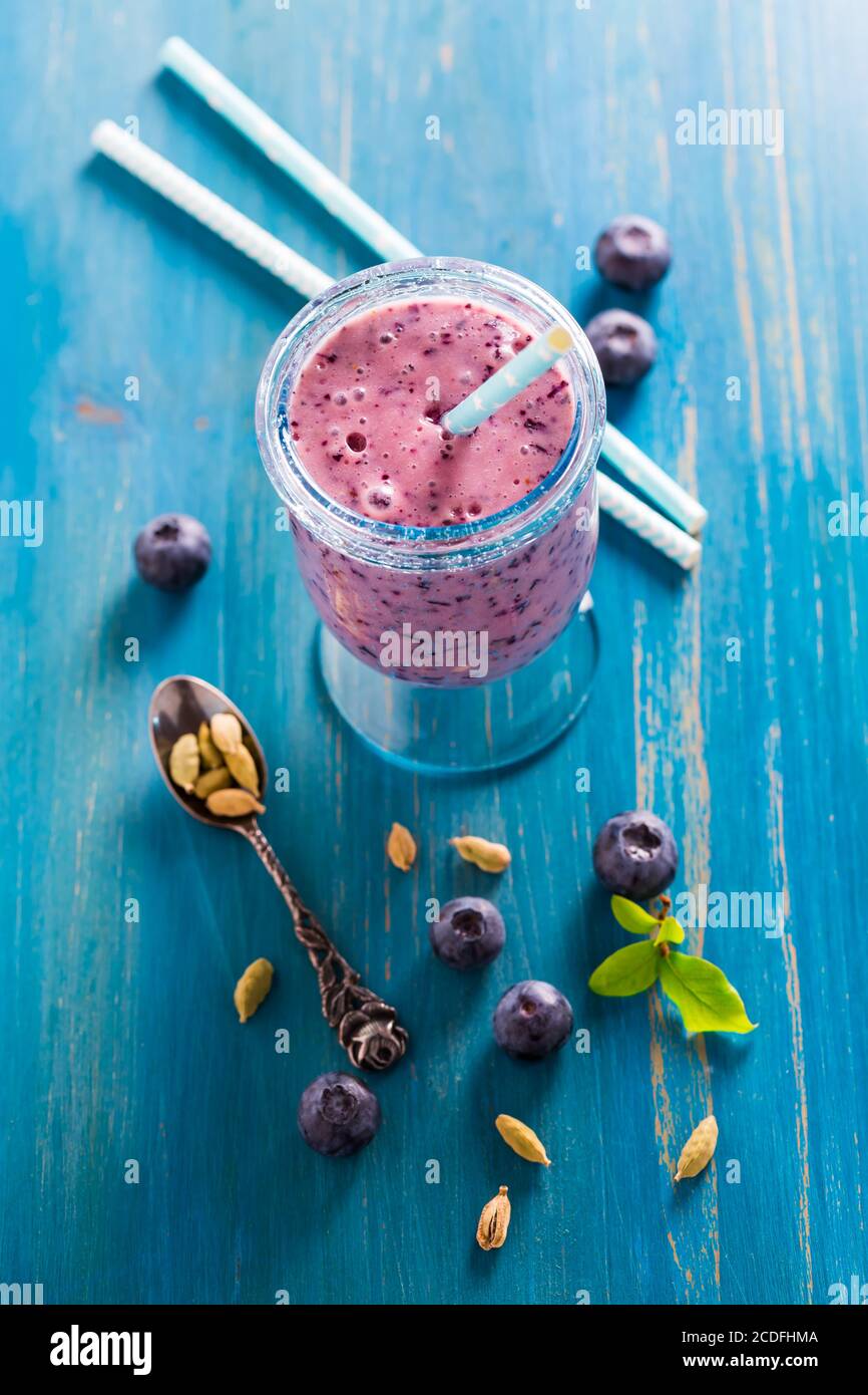 Healthy blueberry lassi or smoothie drink with cardamom on blue wooden ...