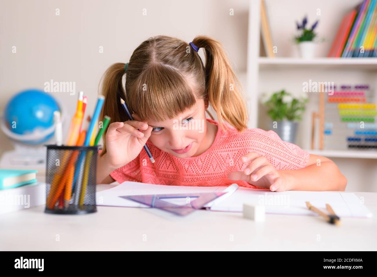 Smiling girl doing homework at home with hand on forehead with school ...
