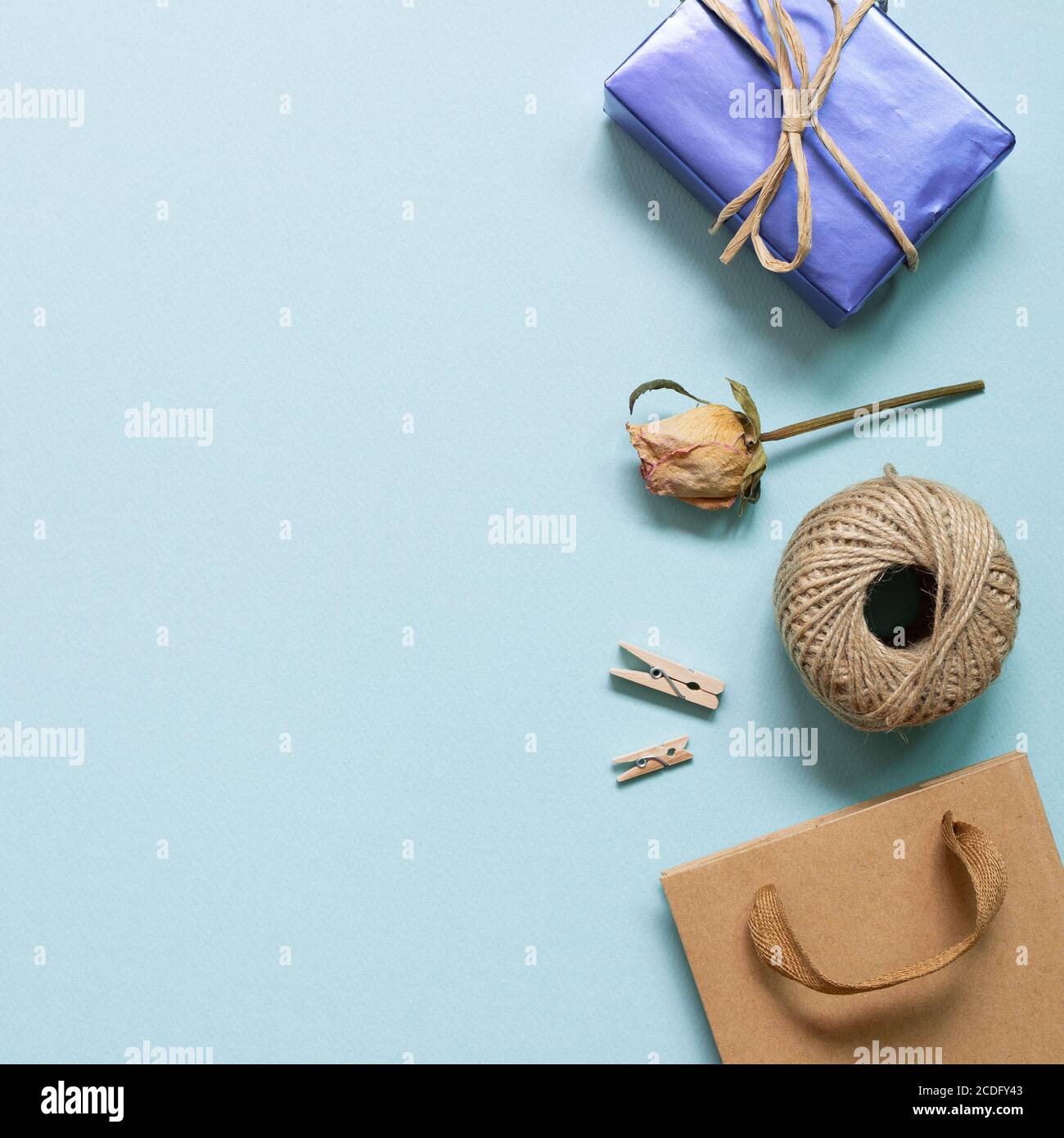 Gift box, string, shopping bag with dry rose flower on blue background ...