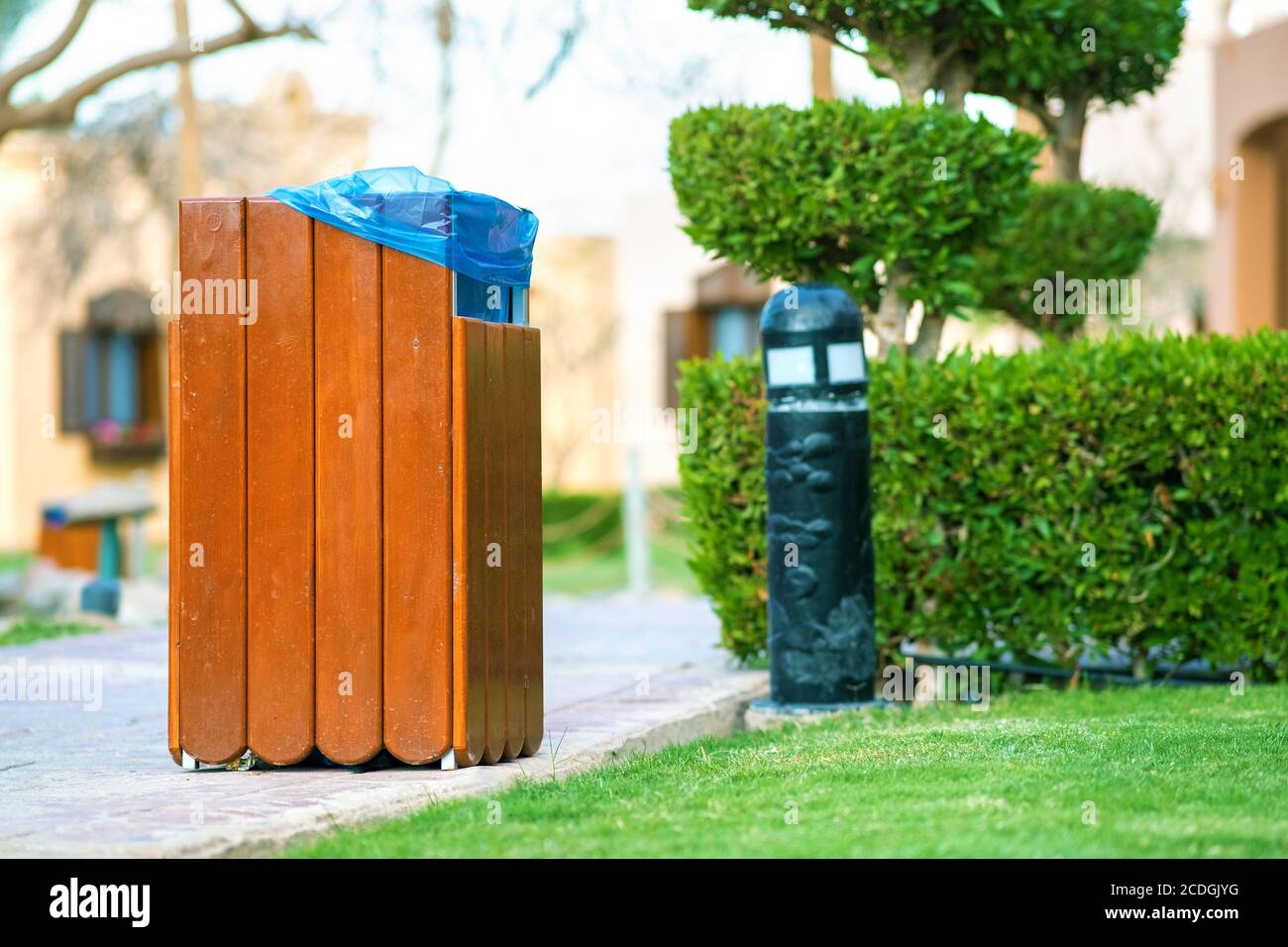 Yellow wooden trash can outdoors on the side of sidewalk in park ...