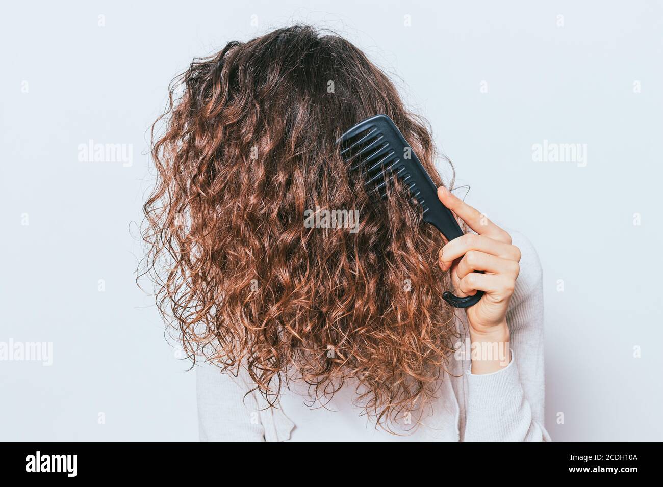 Woman wearing white shirt combing her tangled curly hair on white ...