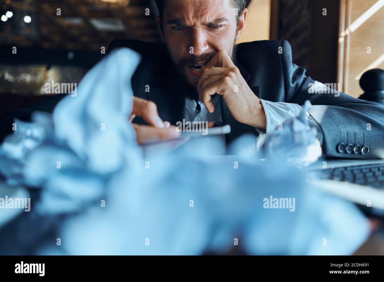 business man sitting at table in front of laptop crumpled paper ...